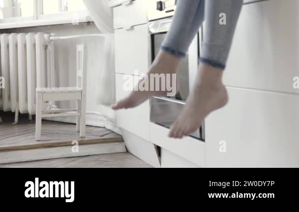 Close up for woman legs dangling with white kitchen drawers and oven on ...