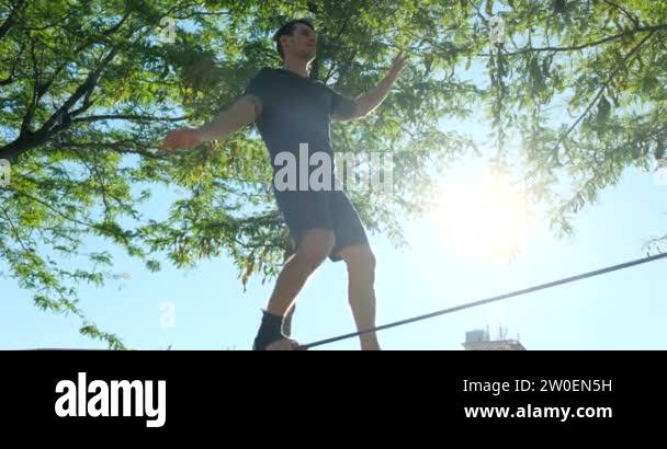 Young man performing as acrobat and training with slackline outdoors ...