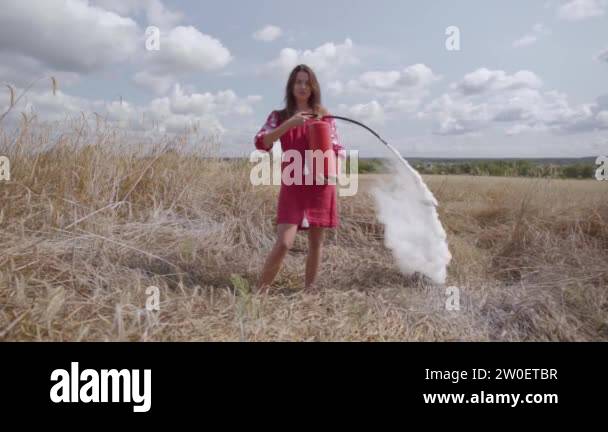 Attractive woman with long hair using fire extinguisher on the wheat ...