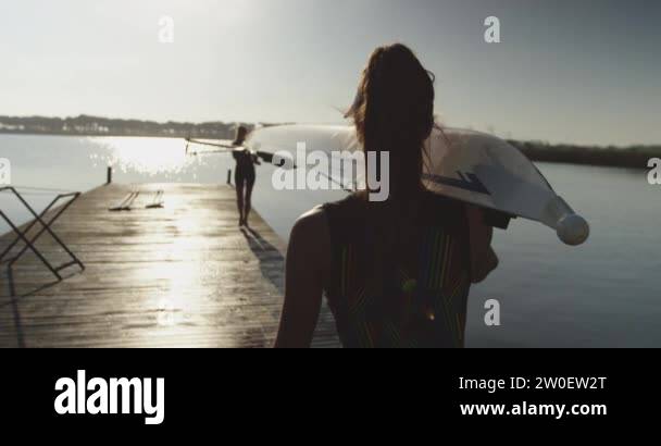 Rear view of two young adult Caucasian female rowers carrying a racing ...