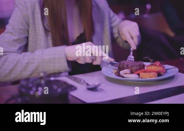 Beautiful young woman eating juicy meat grilled with vegetable in the ...