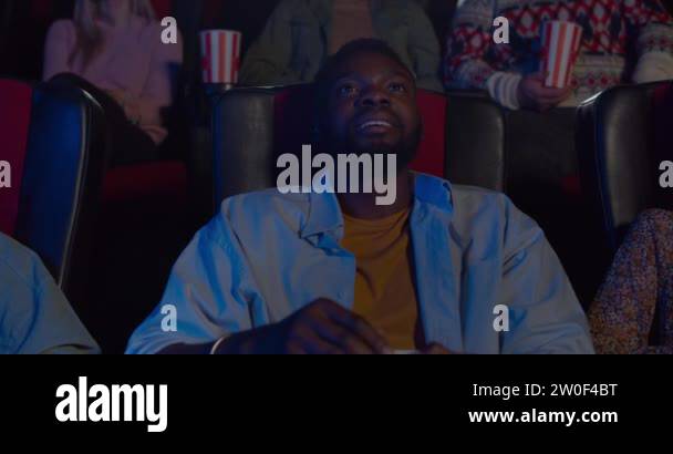 Close up of handsome guy watching action film in cinema. Young african ...