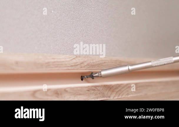 Human hand touches the plastic baseboard with a screwdriver and dowel ...