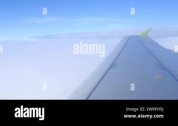 Wing of an airplane descending through thick clouds with a clear blue ...