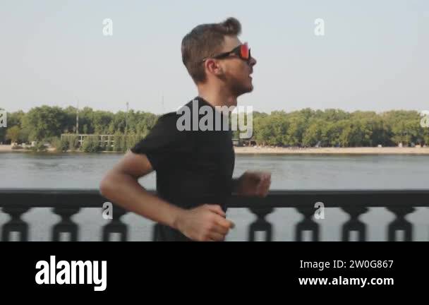 Portrait of active young man runs along city river. Side view of ...