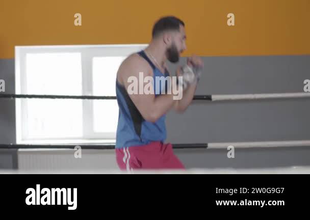 Middle shot of muscular boxer punching air in boxing ring. Side view of ...