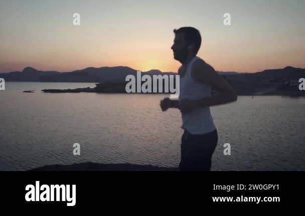 attractive young man running athlete runner training tough cardio exercise workout on calm ocean ...