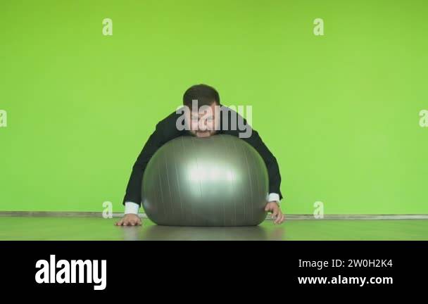 Funny plump man in black suit lies on exercise ball in fitness club or ...