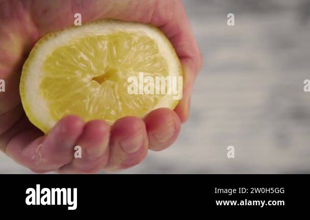Squeezing a lemon with splashes and drops close-up. Hand of a man. On a ...