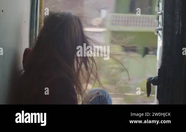 Unrecognizable girl with long waving hair sitting at opened wagon door in indian train. Faceless ...