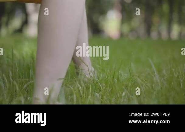 Female legs in yellow dress walking barefoot throw the green grass in ...