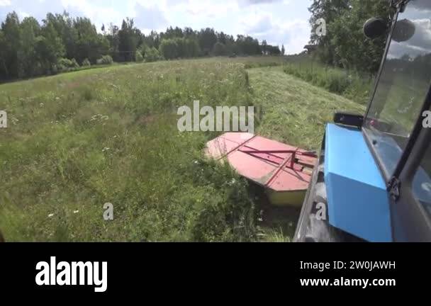 Tractor with rotary mower slowly rides on an inclined field at the end ...