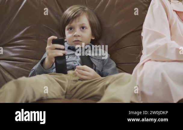 The little cute boy sitting on the leather sofa with legs apart ...
