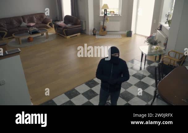 The thief in black clothes and balaclava walking in the large living ...