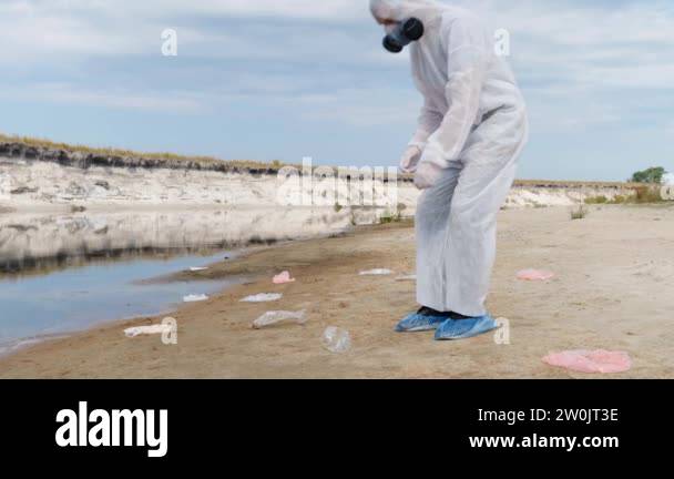 Man in protective suit and respirator picks up discarded plastic trash ...