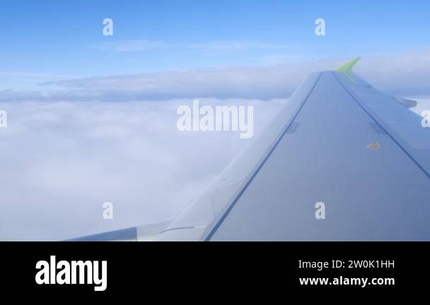 Wing of an airplane descending through thick clouds with a clear blue ...