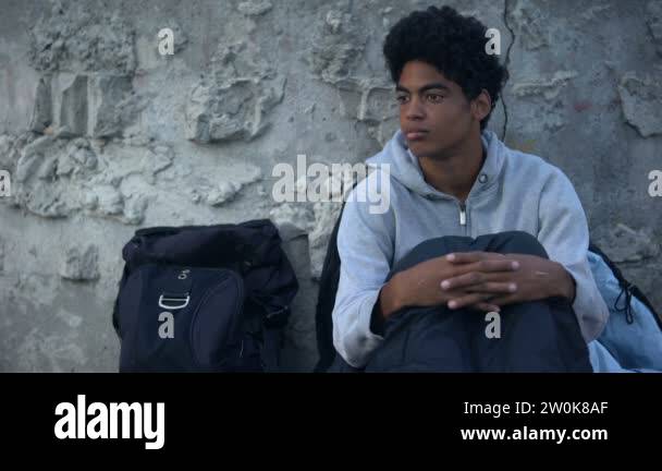 Poor afro-american refugee sitting street with backpack, homelessness ...