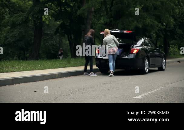 Charming girls open the trunk and pretty blonde puts red emergency stop ...