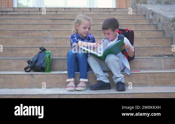 pupils kids with backpacks reading and leafing through a book sitting ...