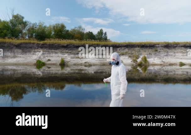 Man in a protective suit and respirator takes tests from polluted river ...