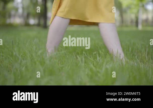 Female legs in yellow dress walking barefoot throw the green grass in ...