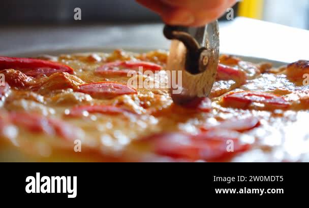 Chef slicing a pepperoni pizza into multiple slices with a pizza cutter ...