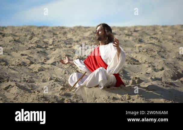 Monk in lotus pose raising hands to sky, praying to god in desert ...