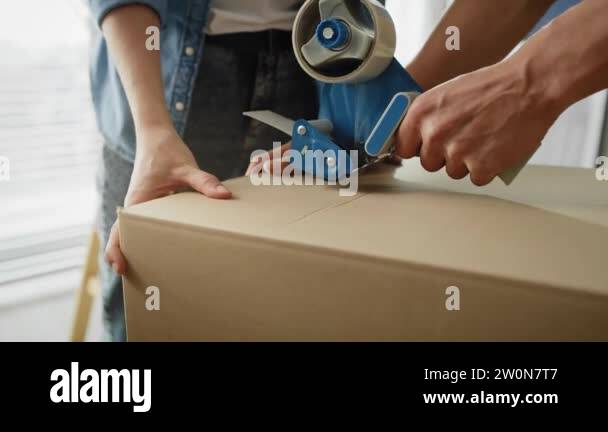 Tracking video of couple packing cardboard boxes while moving house ...
