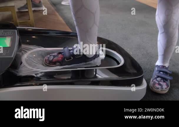 Little girl putting on foot in automatic shoe cover dispenser. Hightech ...