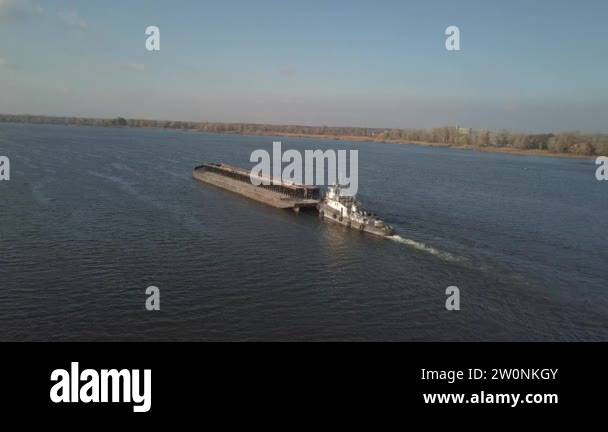 A tugboat ship pushes a barge upstream of the river to transport bulk ...