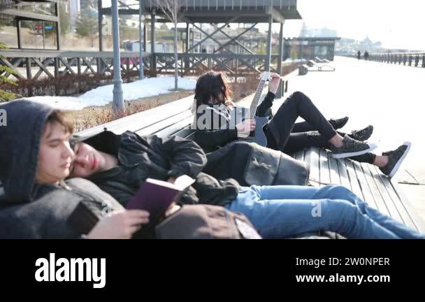 Young friends chilling on a bench - two guys reading a book - a man ...
