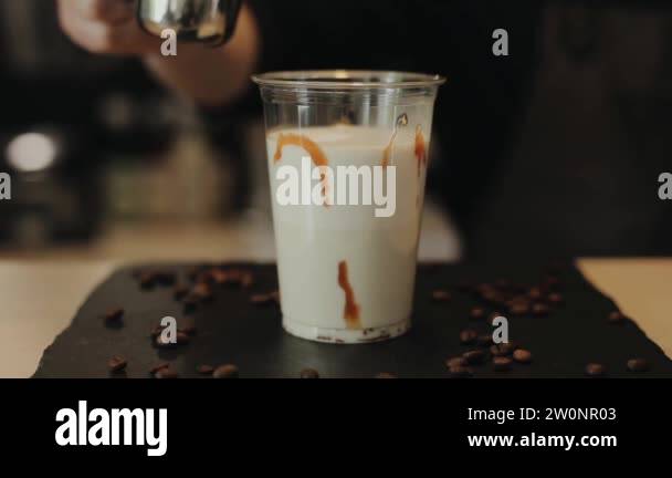 Pouring espresso from a steel pitcher into a plastic cup with milk ...