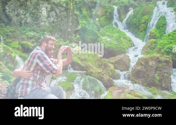 Two friends are taking photos in front of the waterfalls. They're happy ...