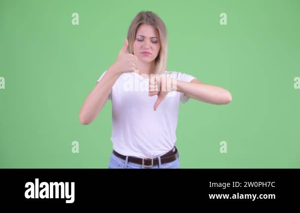 Confused young blonde woman choosing between thumbs up and thumbs down ...