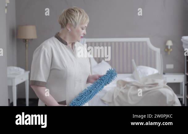 Exhausted professional maid looking back at bed in hotel room and ...