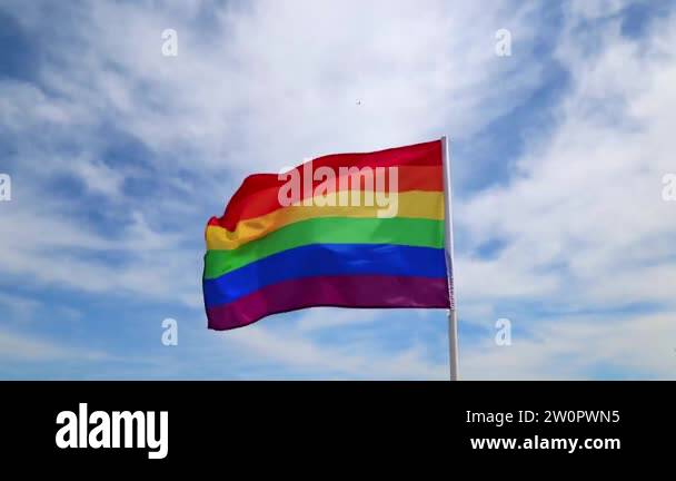 Realistic rainbow flag of an LGBT organization waving against a blue ...