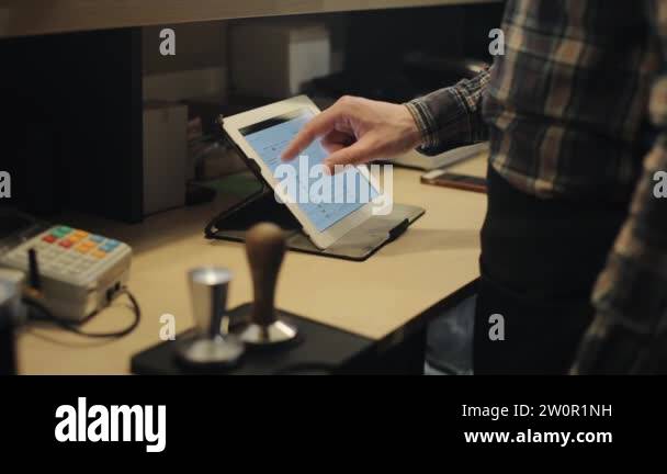 A close-up of a male cashier using a touch pad behind a counter in a ... A close-up of a male cashier using a touch pad behind a counter in a ...