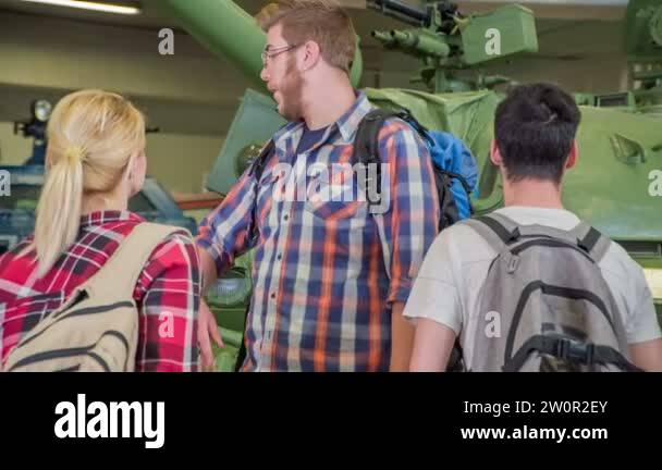 A young man points at the military tank in a museum. Two friends are ...