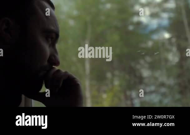 Man looking out window with chin on hand in a train, serious expression ...
