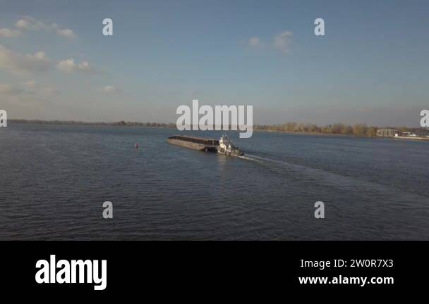 A tugboat ship pushes a barge upstream of the river to transport bulk ...