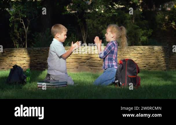 merry schoolkids playing clapping game sitting on grass after learning ...
