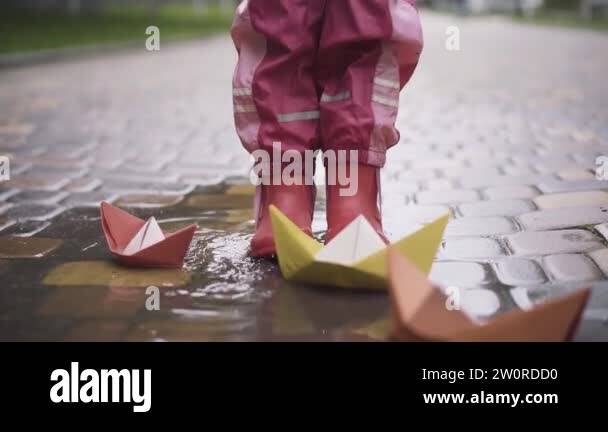 Feet of little girl in rubber boots stomping in puddle with paper boats ...