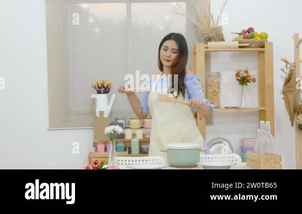 4K. beautiful Asian woman hold ladle dancing in the kitchen , feeling enjoy for cooking behind ...