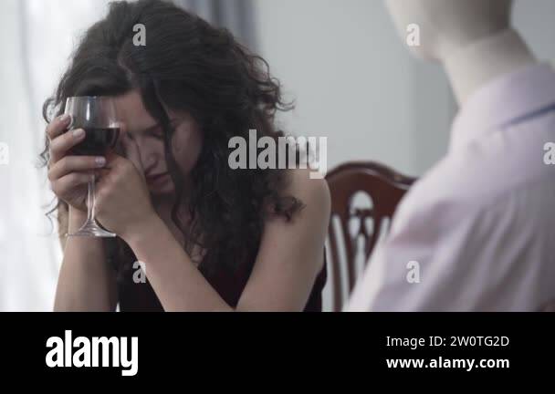 Cute crying curly woman sitting at the table drinking red wine with a ...