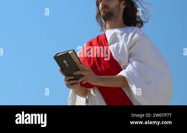 Jesus Christ in robe and sash raising Holy Bible to heaven, praying God ...