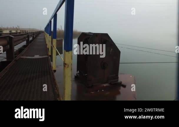 Metal floating bridge over river, early in morning with fog and dew ...