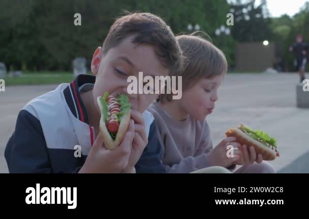 Two little kid boys eating hot dogs outdoors. Siblings enjoying their ...