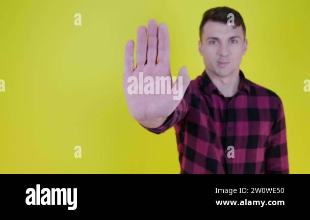 Man raises hand, shows palm to the camera and says stop on a yellow ...