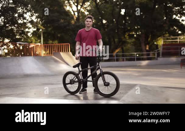 A young man with a BMX bike stands next to his bike with ramp, skate ...