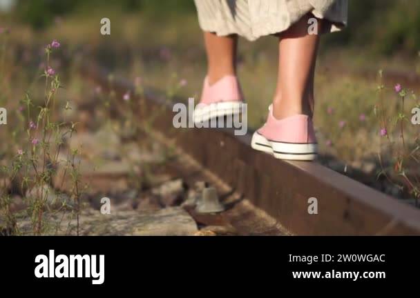 Girl walking along railroad rail. Romantic slow motion tracking shot of ...
